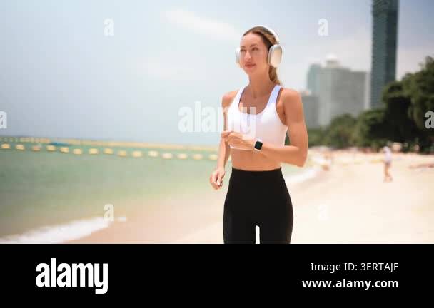 A fit woman with headphones is running on a sandy beach next to the ...