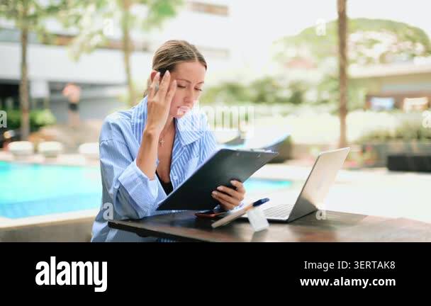 A woman is sitting at a table outdoors, looking stressed while ...