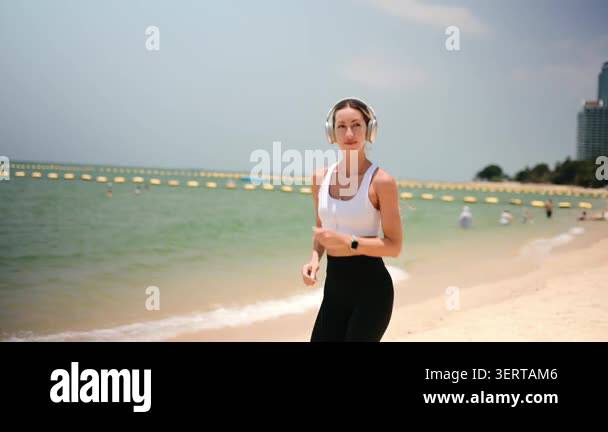 A woman with headphones is running on a sandy beach next to the ocean ...