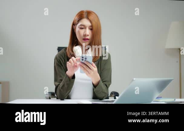 A young woman with headphones around her neck is sitting at a desk and ...