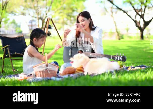 A woman plays guitar while a young girl interacts with a small dog ...