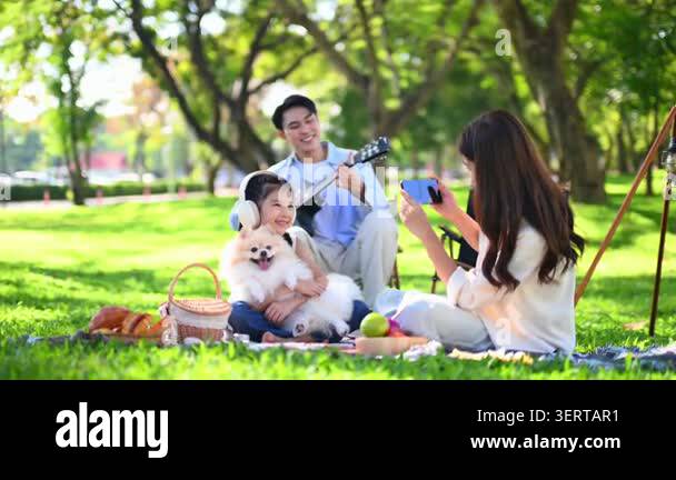A family enjoys a picnic in a park, with the father playing guitar and ...