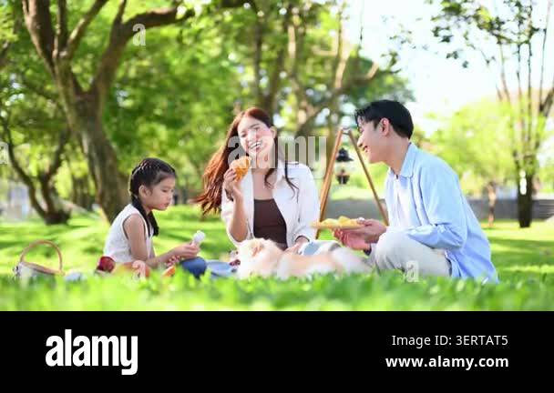 A family enjoys a picnic in a park with their dog, sharing food and ...