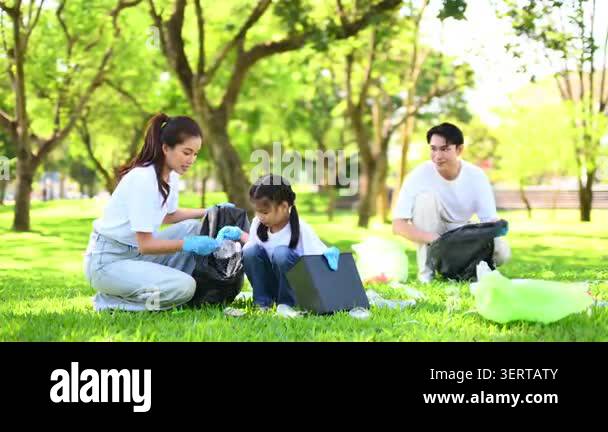 A family is cleaning up litter in a park, collecting trash in bags. The ...