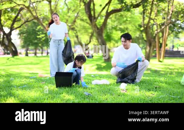 A family is cleaning up litter in a park, collecting trash in bags on a ...