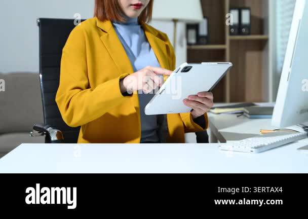 A woman in a yellow jacket is using a tablet computer while sitting at ...