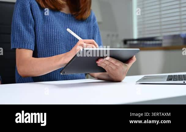 A woman's hands holding a tablet and stylus, actively drawing or ...