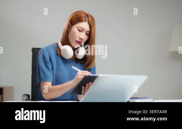 A young woman with headphones around her neck is focused on her tablet ...