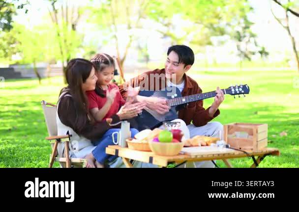 A happy family enjoys a picnic in the park, with the father playing the ...