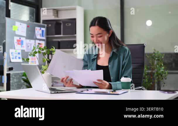 A woman is sitting at a desk, reviewing documents and celebrating ...