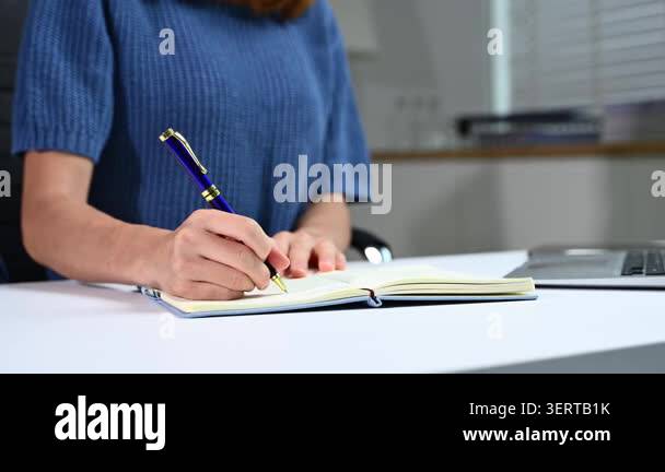 Close-up of a woman's hands writing in a notebook with a pen while ...