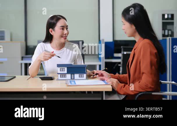 Two women are discussing a house model and contract at a desk in an ...