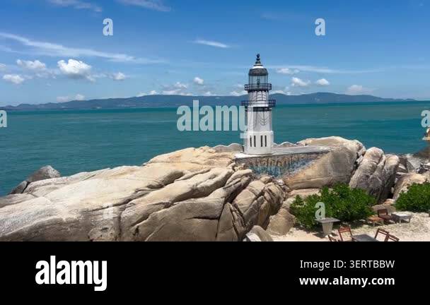 Small lighthouse is located on a rocky shore under a blue sky with a ...
