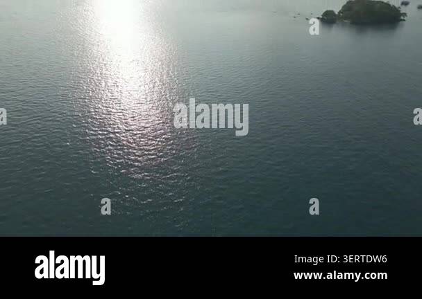 Aerial over a vast glittering open sea with a tiny distant island ...