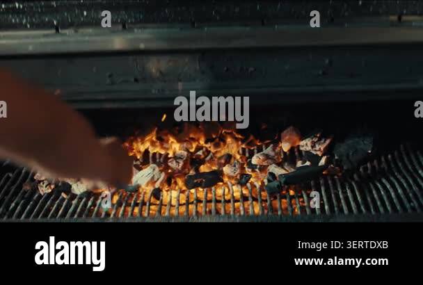 Close-up of hand adjusting charcoal on grill. Flames and sparks rise ...