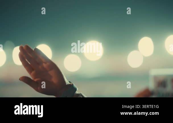 Hand raises toward bright lights. Blurred spots form a bokeh effect ...