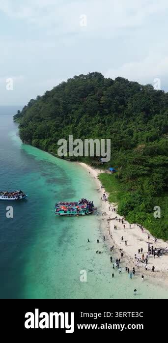 Vertical aerial of a jungle island beach crowded with tourists and tour ...