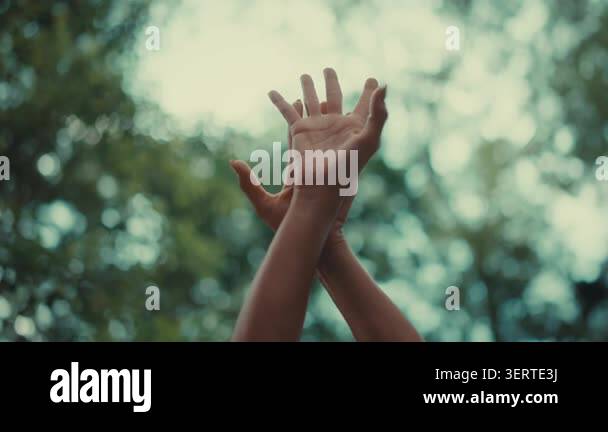 Two hands clap softly in the air. Green forest background is blurred ...