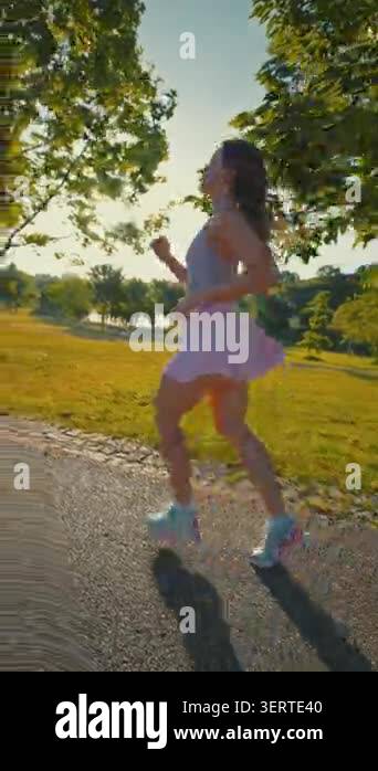 Fit young woman with long hair jogging on a path in a park at sunset ...