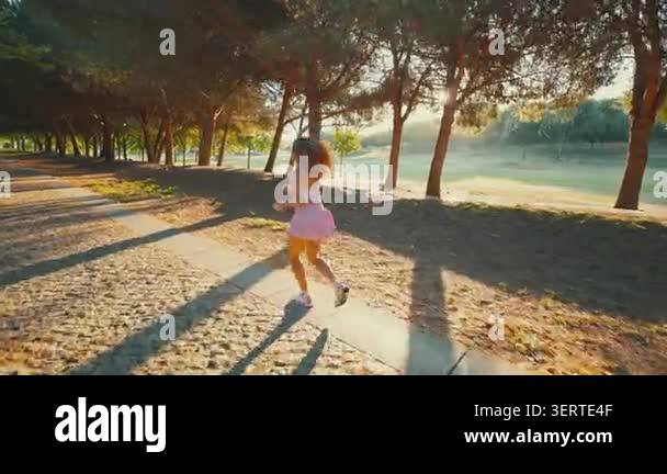 Back view of a young fit woman jogging along a park alley at beautiful ...
