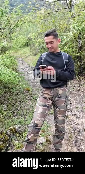 Young man in camouflage pants standing on a mountain path while using ...