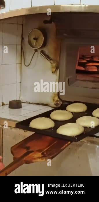 Skilled baker placing raw dough buns into a hot, traditional oven using ...