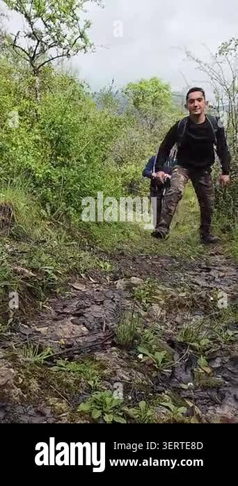 Two male friends walking uphill on a steep, muddy path during a trek in ...