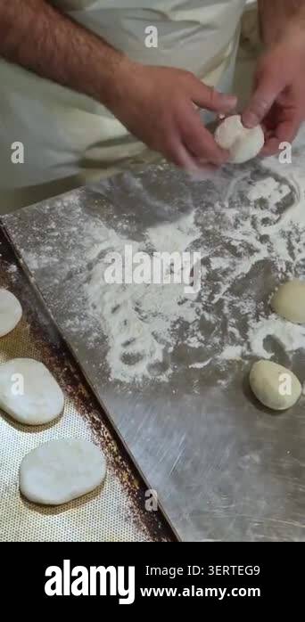 Bakers hands skillfully shaping dough balls on a floured steel surface ...