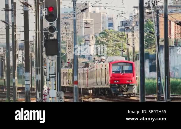 A red train pulls into a busy station with many tracks and signals ...