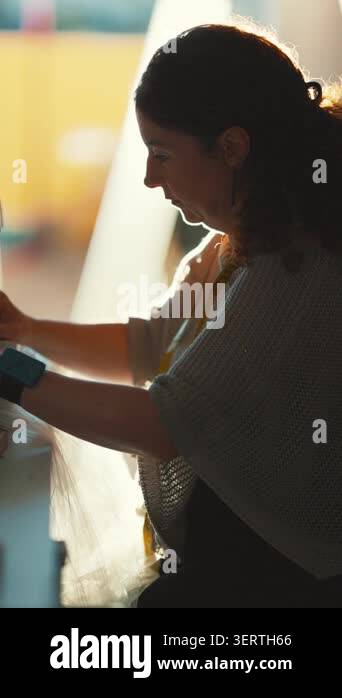 Focused tailor working with fabric on a sewing machine in her sunlit ...