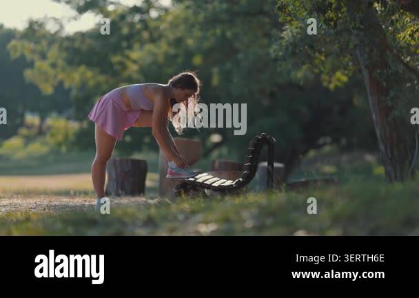 A woman ties her shoelaces while standing on one leg next to a park ...