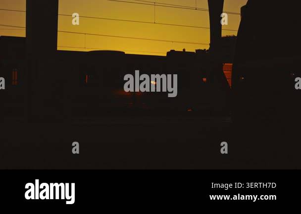 A train waits at the station during sunset. The sun shines behind the ...