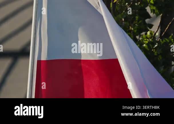 A flag of Poland is shown waving gently in a public area. The colors ...
