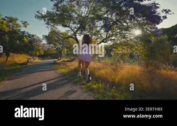 A woman is running along a pathway in a park filled with green trees ...
