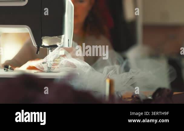 Dressmaker guides delicate white fabric through a sewing machine in a ...