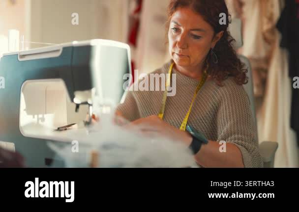 Focused female tailor working with a sewing machine on a garment in a ...