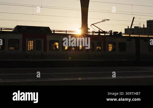 A train travels through an urban area at sunset. The sun shines behind ...