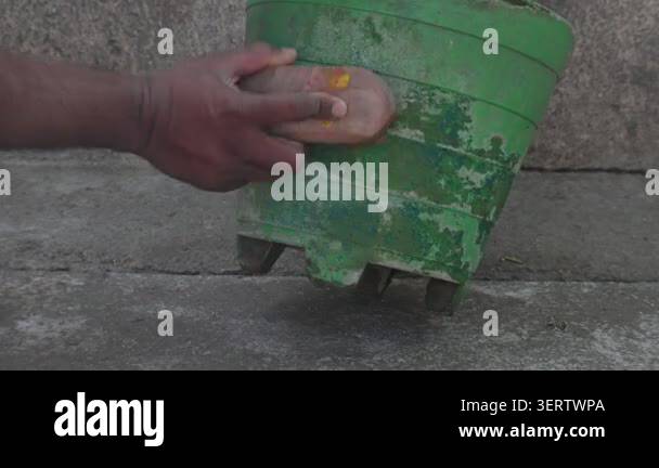 A person is cleaning a green cement flowerpot by hand using a coconut ...
