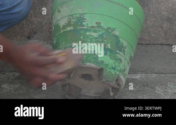 A person is cleaning a green cement flowerpot by hand using a coconut ...