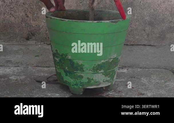 A person uses a paintbrush to apply red paint over a green cement pot ...
