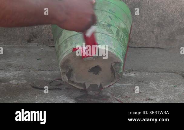 A person uses a paintbrush to apply red paint over a green cement pot ...