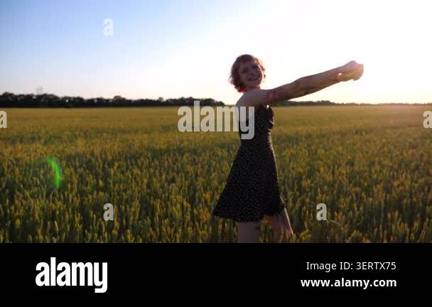 Young female hipster in dress posing on camera on green barley field at ...