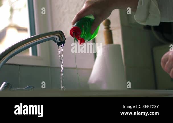 Woman pouring washing up liquid into kitchen sink medium zoom slow ...