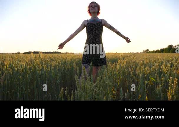 Pretty hippie girl in dress standing on green barley field and raising ...