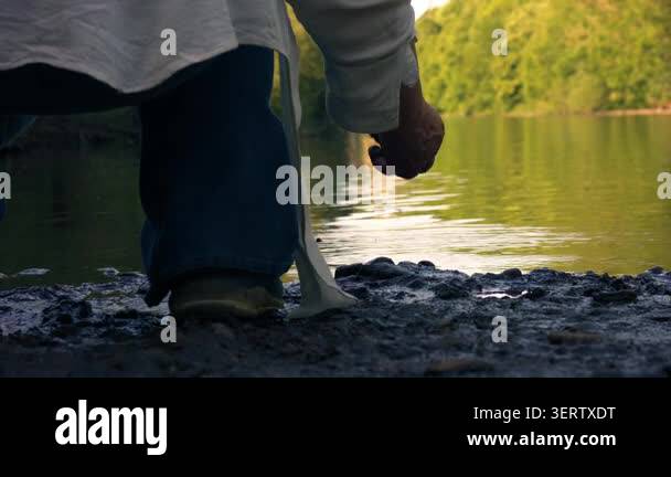 Woman by riverside throws stone into water medium zoom slow motion ...