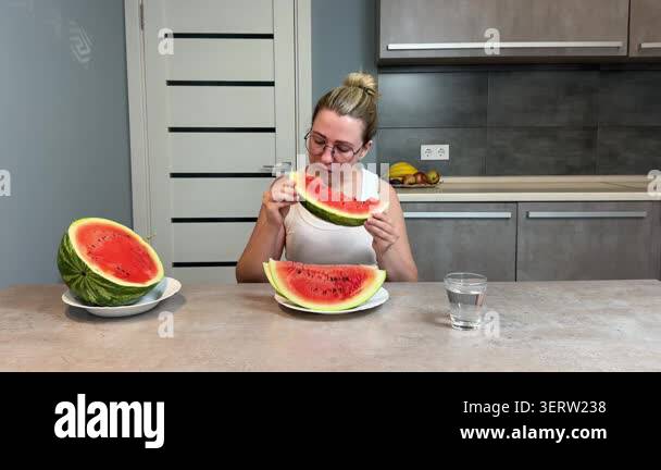 A casually dressed woman with glasses and a top bun sits at a kitchen ...