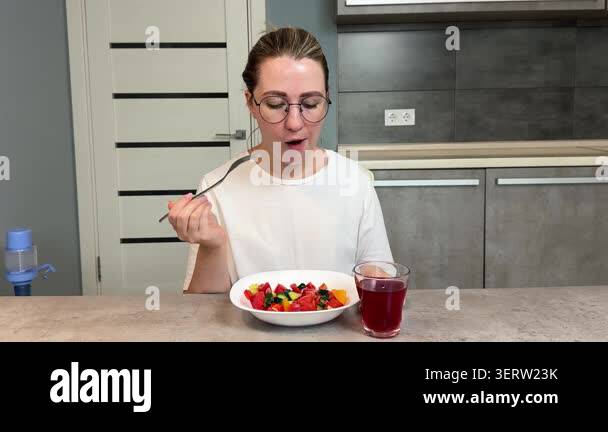 A young woman sits at a kitchen island in a modern home kitchen, eating ...