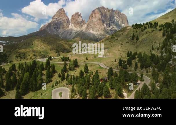 A winding road curves through a green alpine valley with pine trees ...