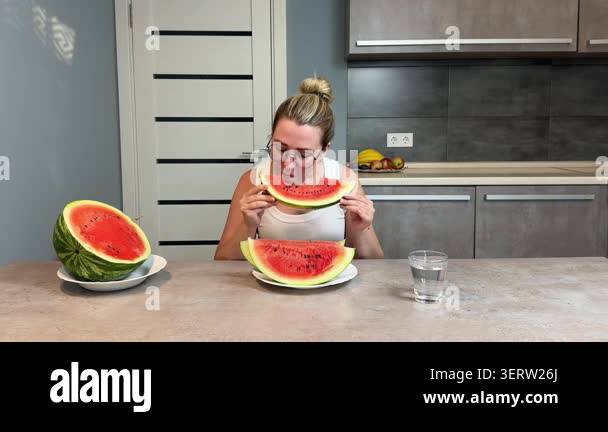 A young woman sits at a kitchen island holding a large half-moon slice ...