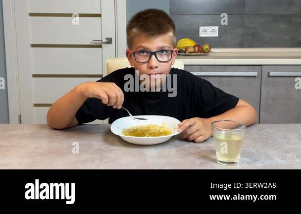 A young brown-haired boy wearing glasses and a black t-shirt sits ...